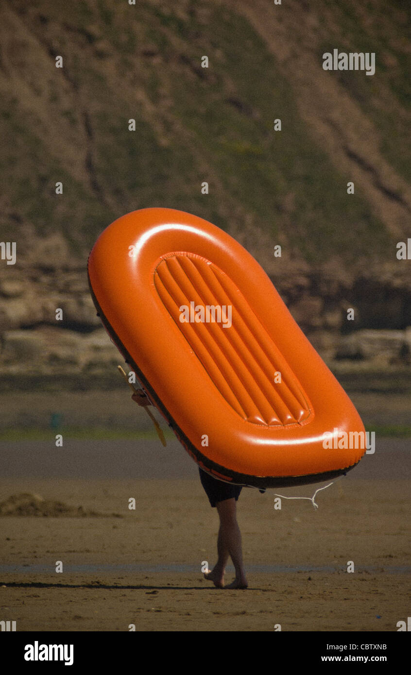 Rear view of a caucasian man carrying an orange coloured inflatable ...