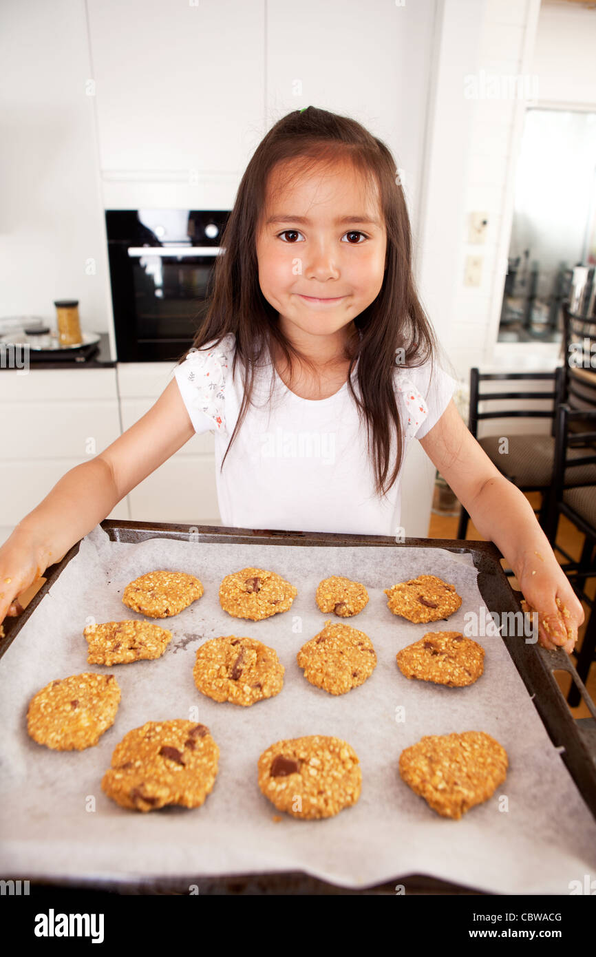 Cute young girl looking at camera with bakng sheet full of raw cookies ...