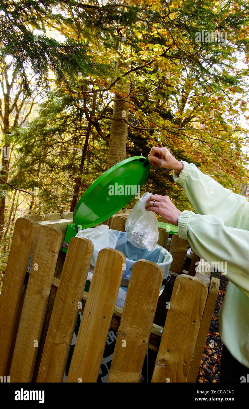 Person disposing of waste in a green bin surrounded by autumn trees in ...