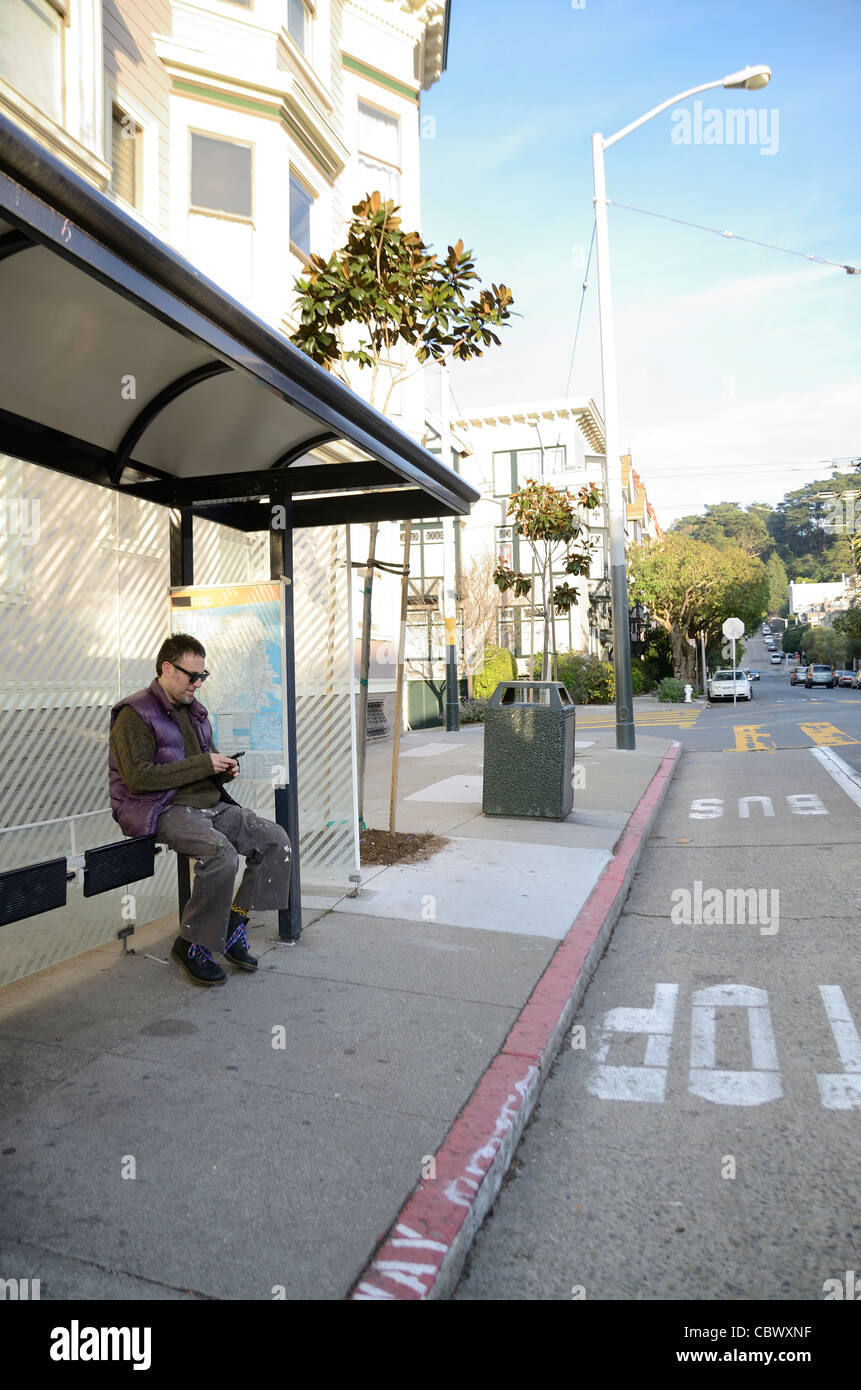 A main checking his cellphone while waiting at a bus stop Stock Photo ...