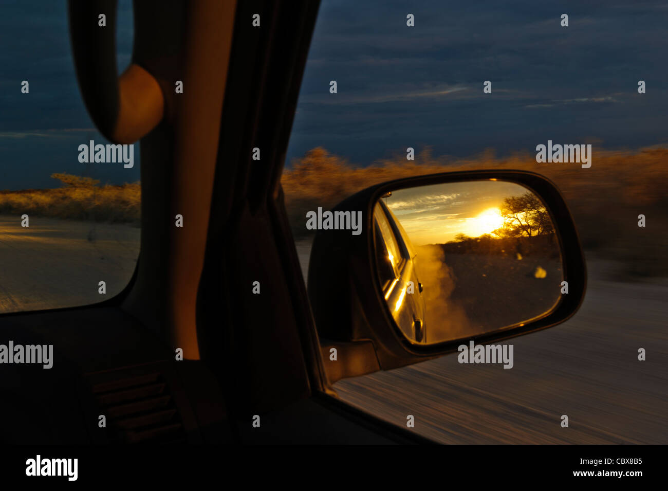 Descending sun, seen in rear-view mirror when driving on a gravel road ...