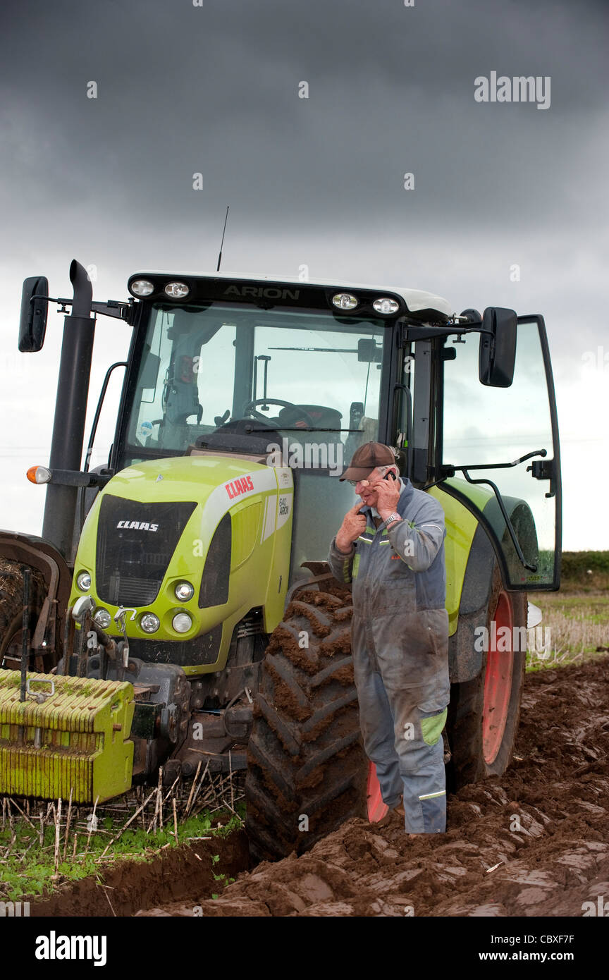 Farmer talking on mobile phone whilst standing in front of stationary ...