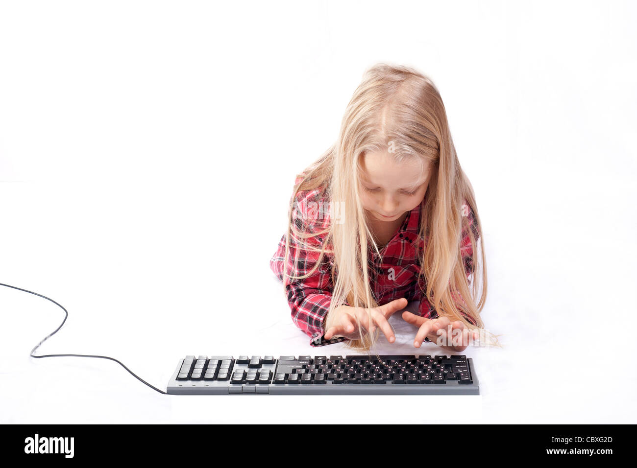 Little girl writes on a computer keyboard against white background ...