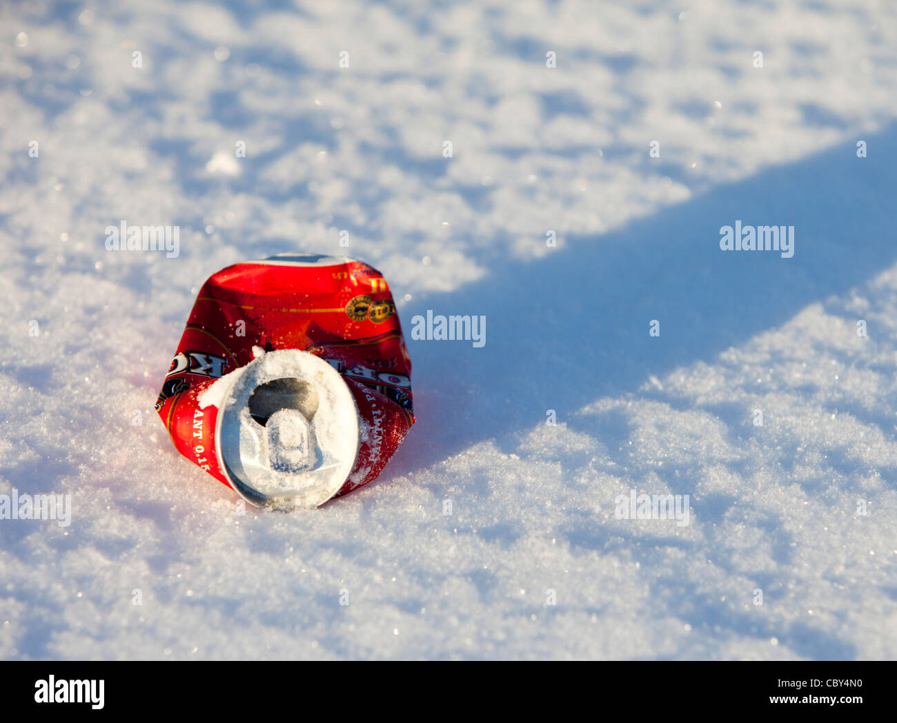 Isolated closeup of crushed red beer can lying on ground on snow at ...
