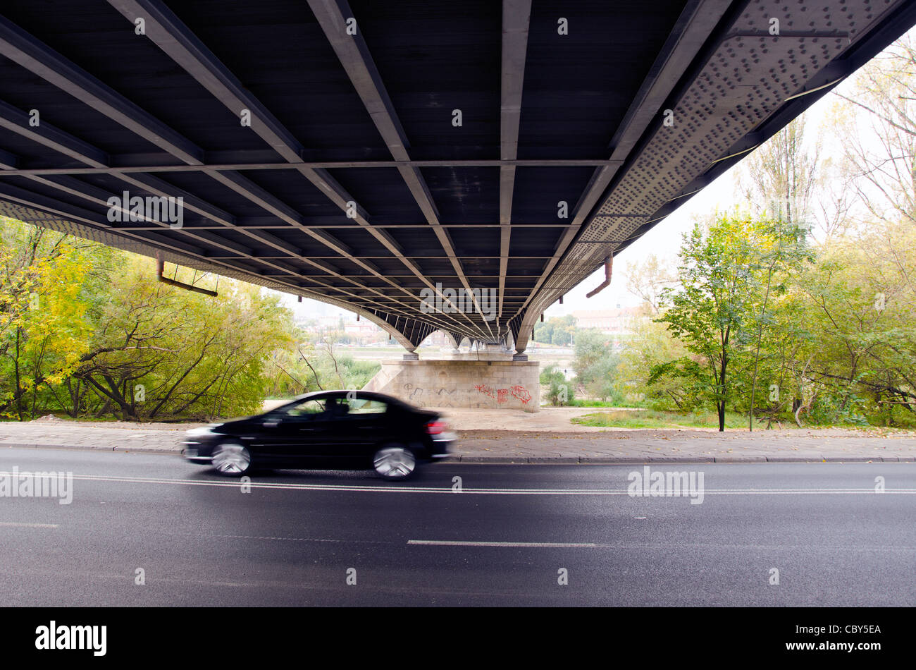 Bridge underneath over the river and road and black car going fast out ...