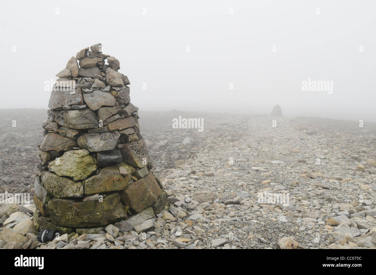 This image shows two cairns on top of Ben Nevis, Scotland, along a path ...
