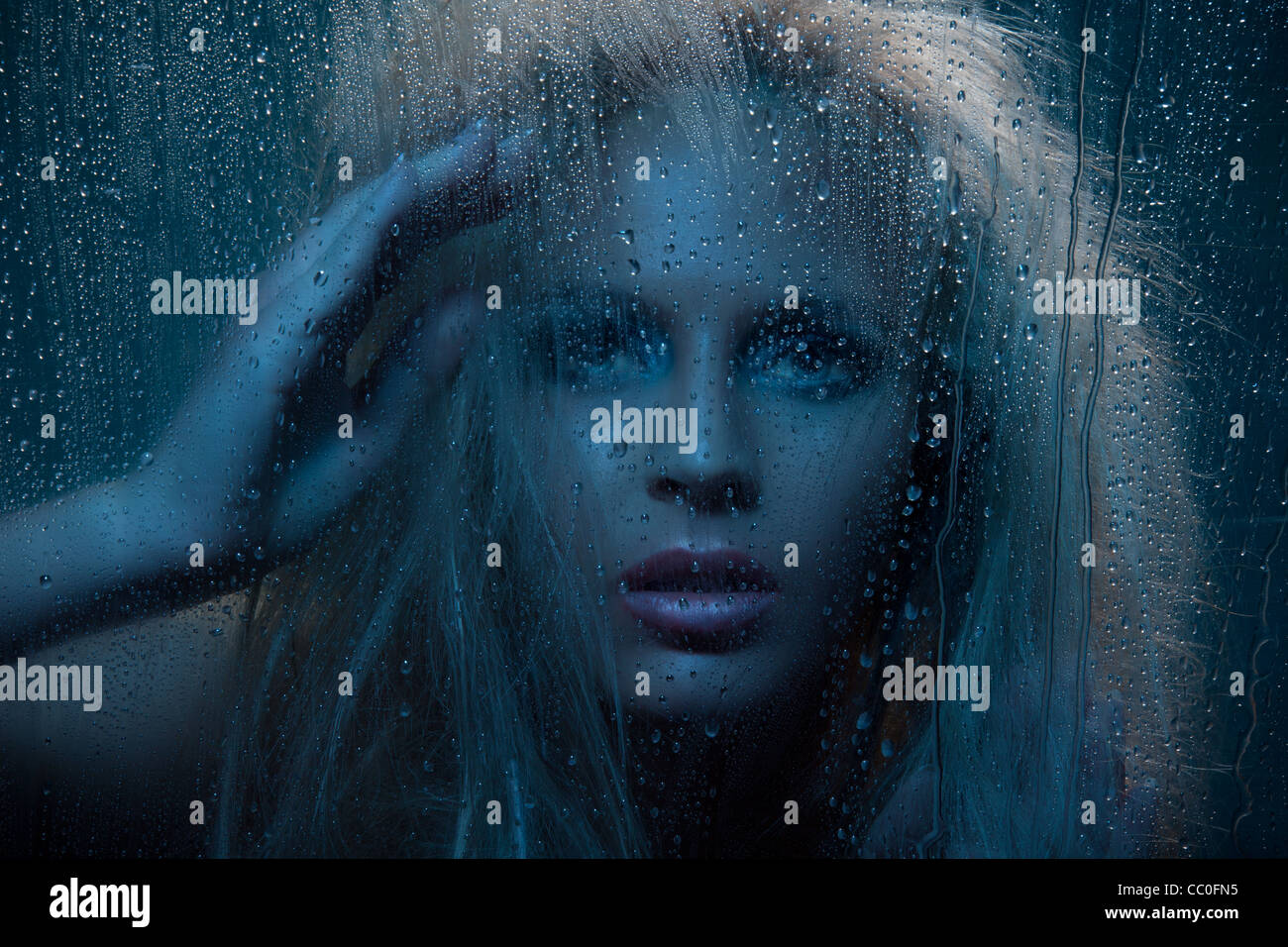 Beautiful confident woman looking through window with rain drops on it ...