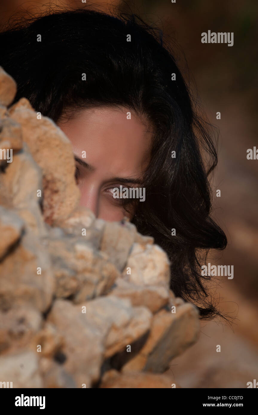 Serious young woman hiding behind rocks Stock Photo - Alamy
