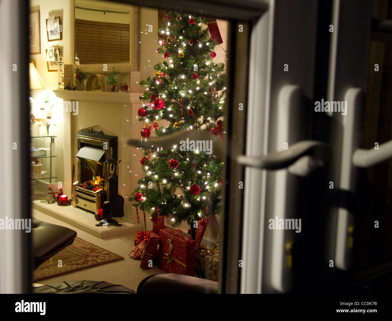 A Christmas tree and presents in a room, viewed from outside through a ...