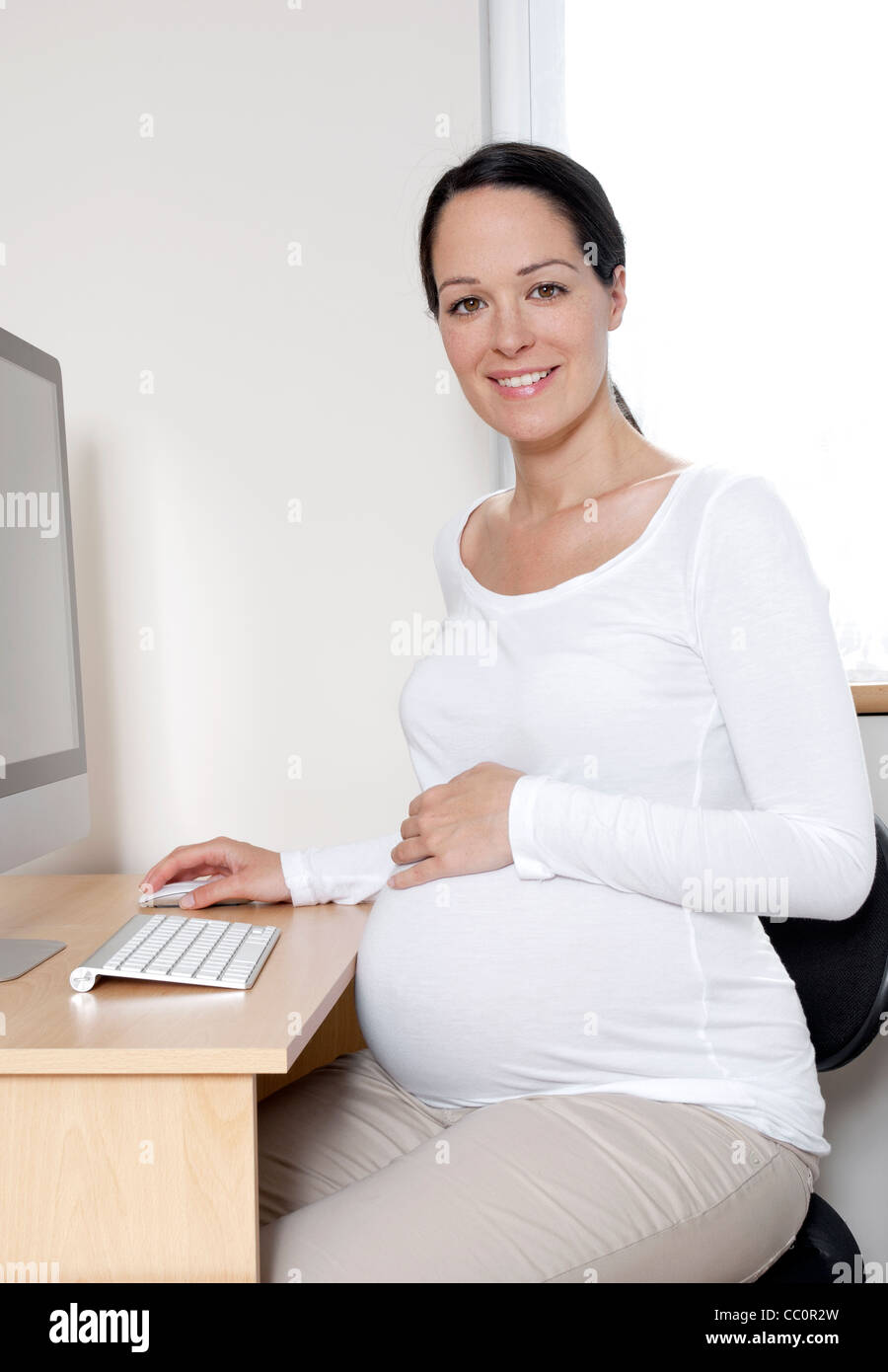 Pregnant woman sitting at computer desk smiling Stock Photo - Alamy