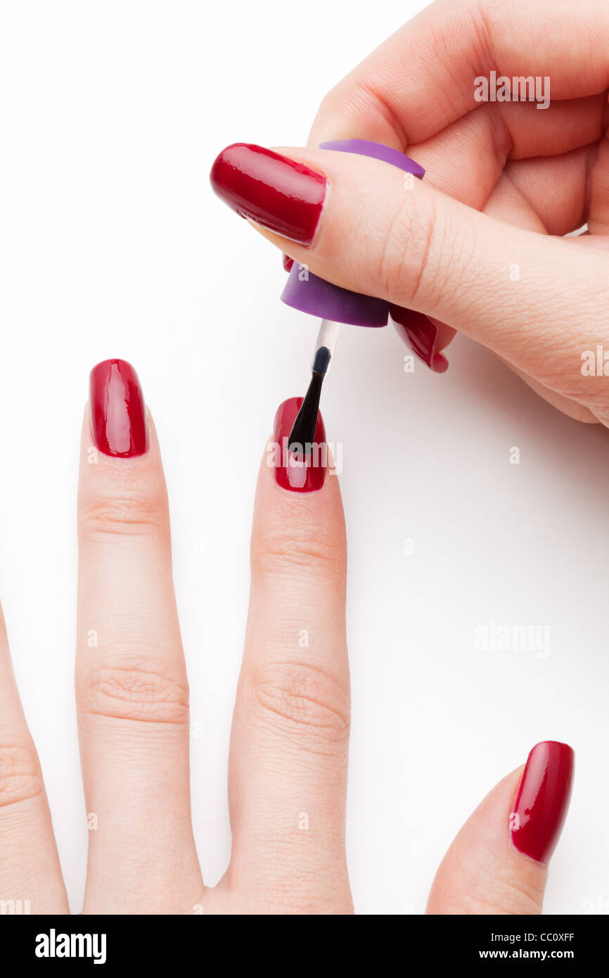 Painting female fingernails with red enamel close-up on white ...