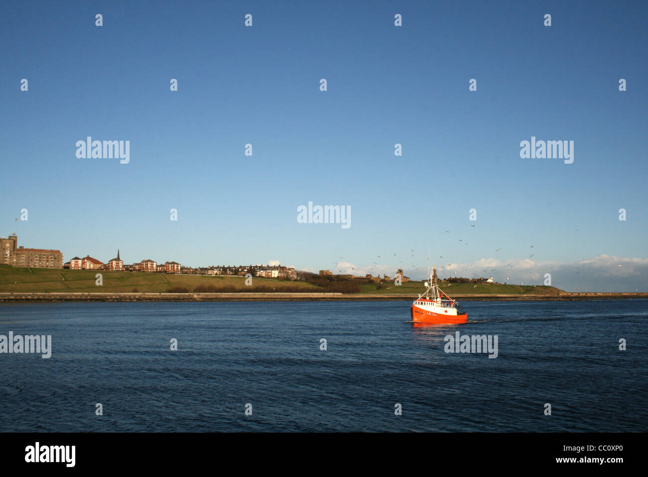 A fishing boat enters the River Tyne with Tynemouth in the background ...