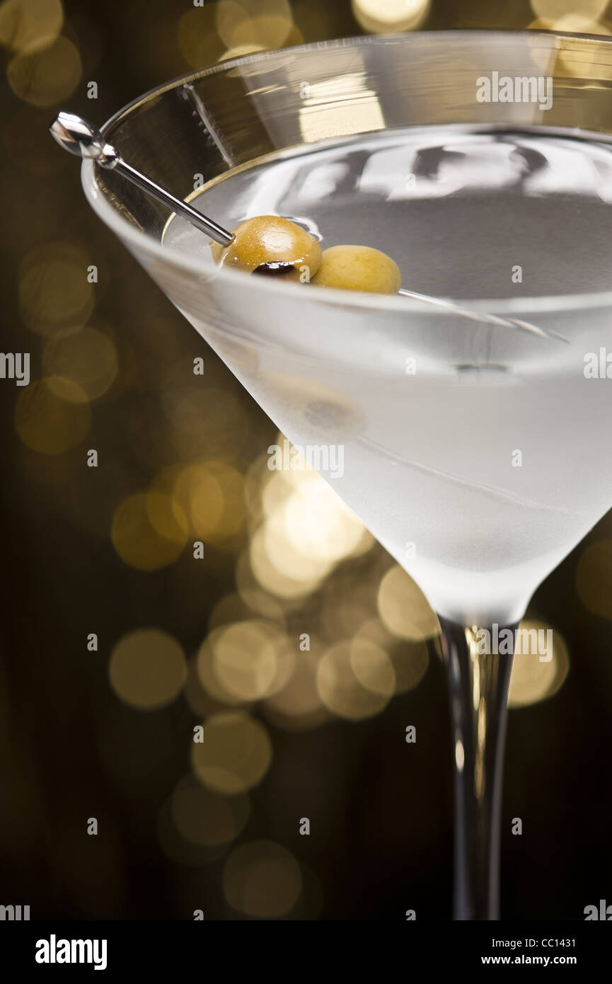 Vodka Martini with olive garnish in front of a gold glitter background ...