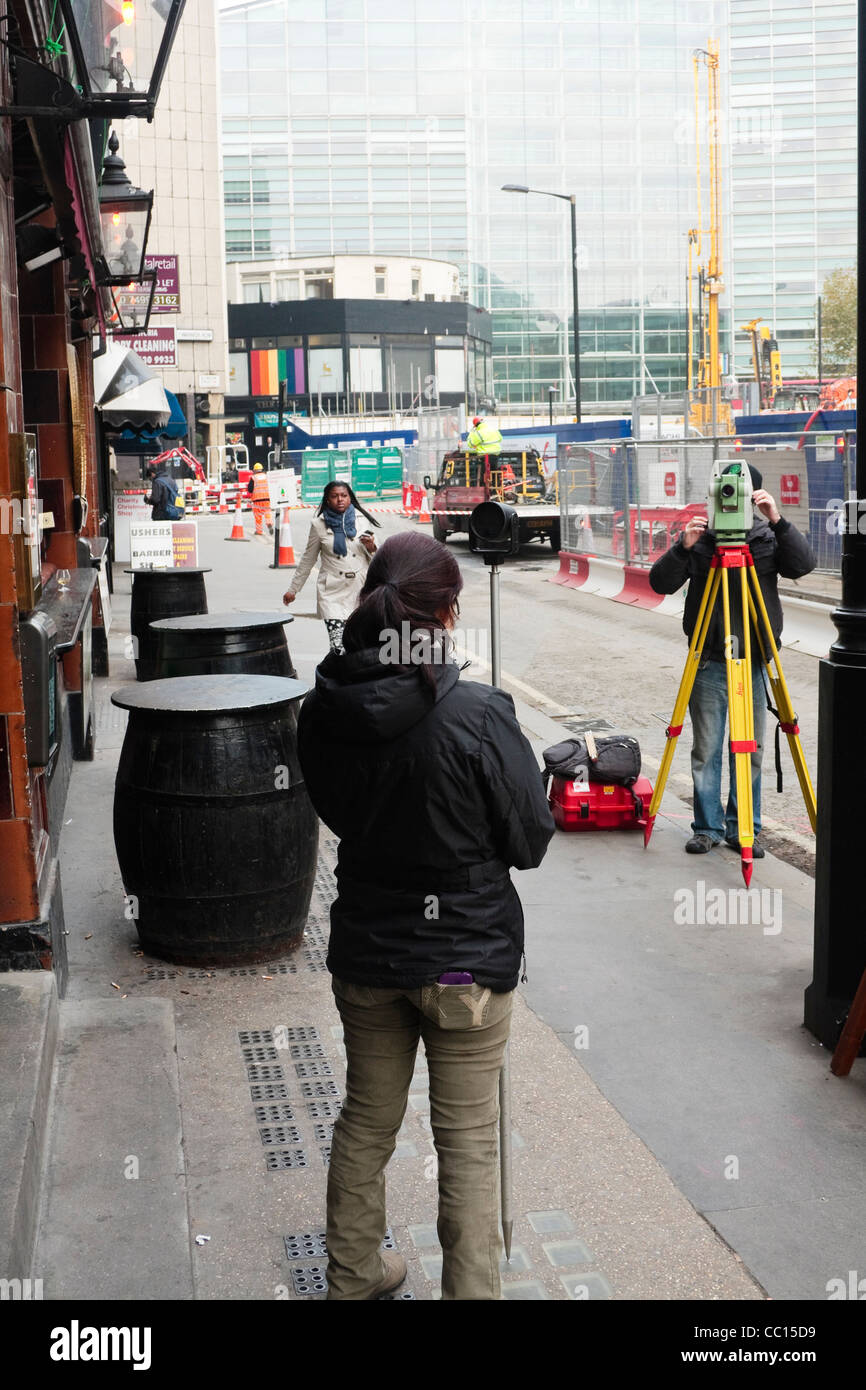Two surveyors using an auto levelling tool survey an area outside a ...
