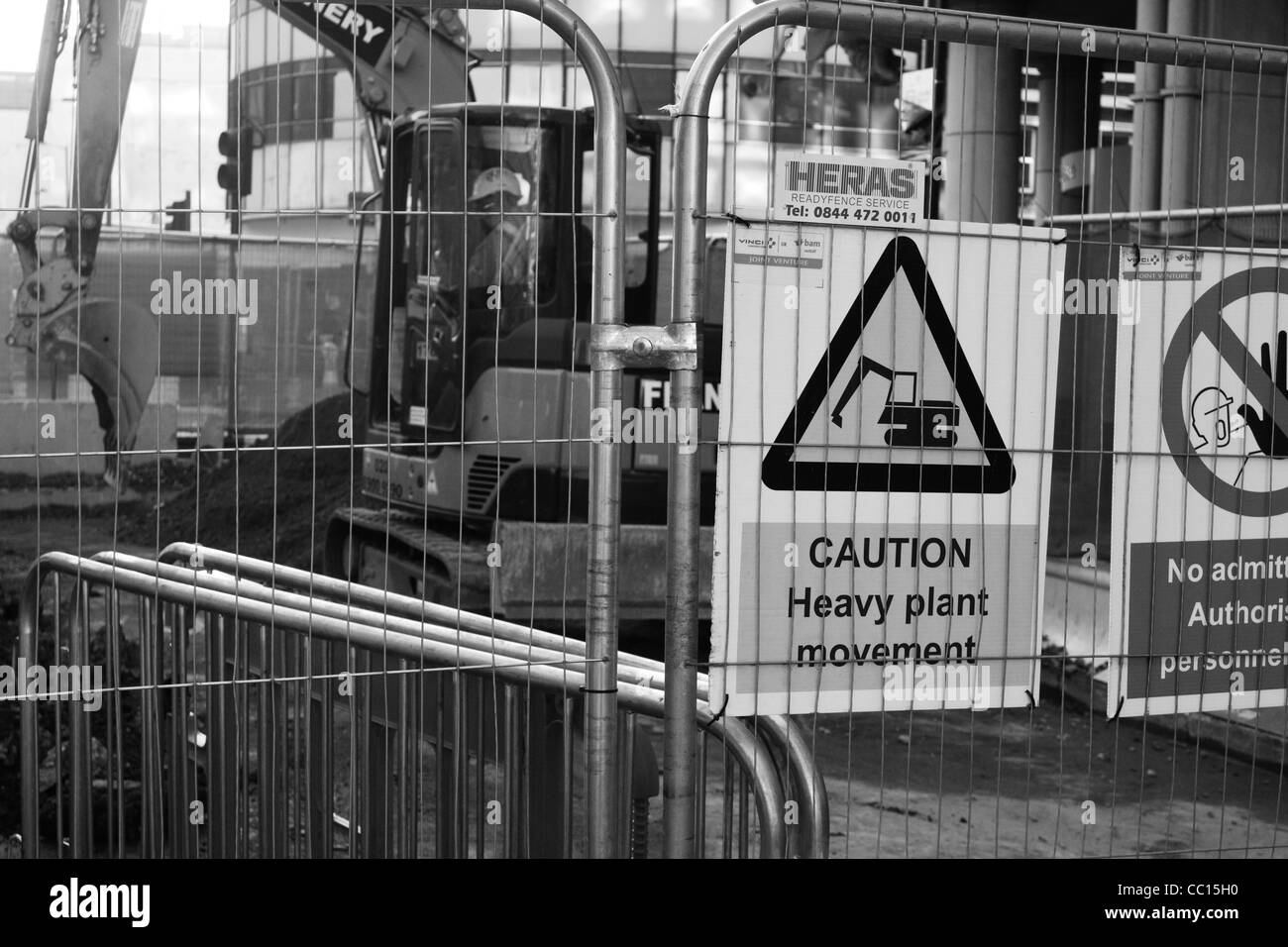 A man operates a digger on a building site behind a safety fence Stock ...