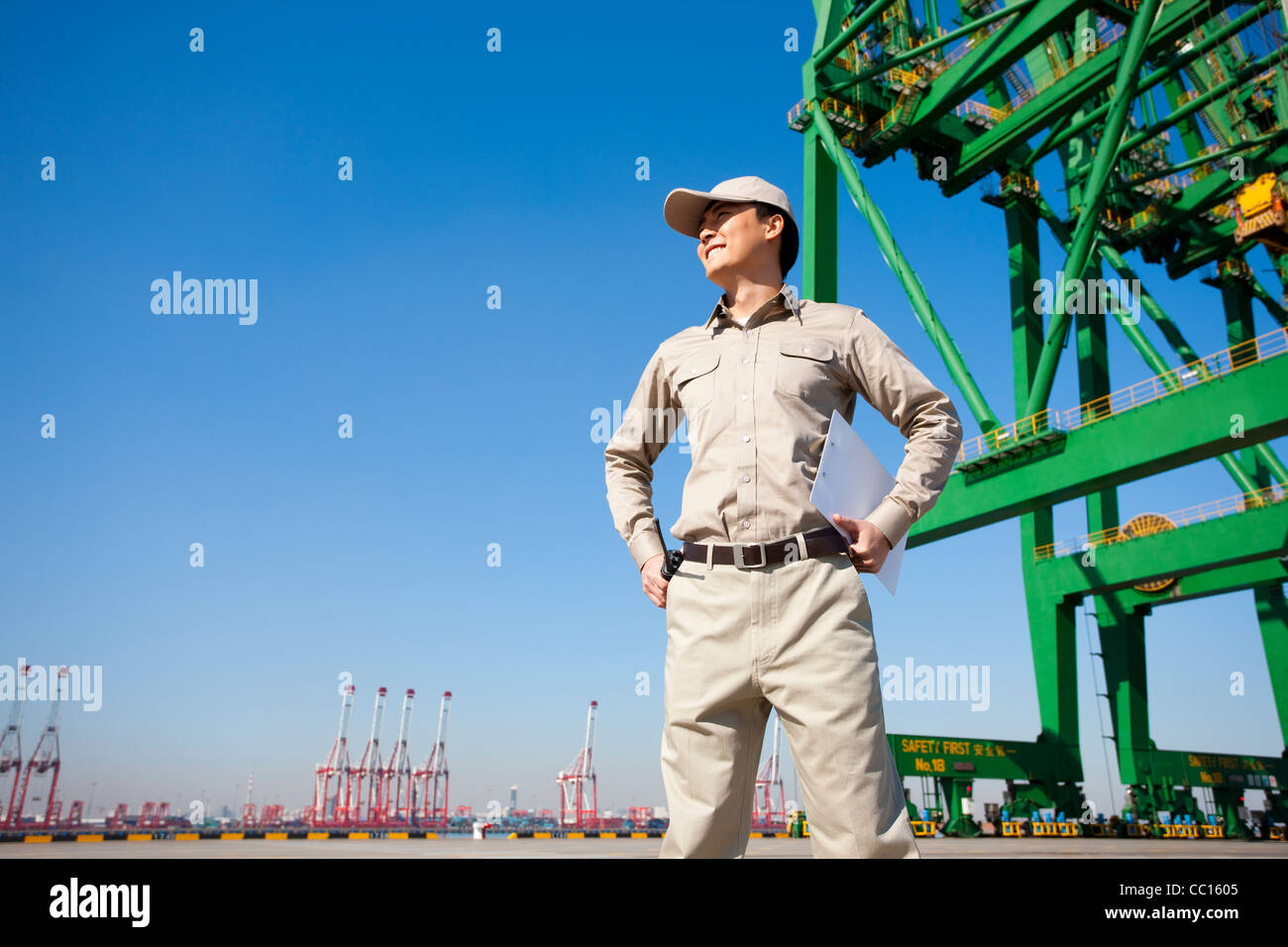 Male shipping industry worker with hands on hips with shipping dock ...