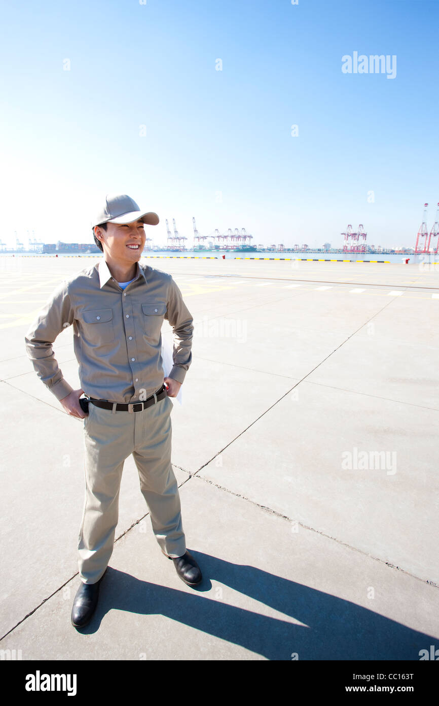 Male shipping industry worker with hands on hips with shipping dock ...