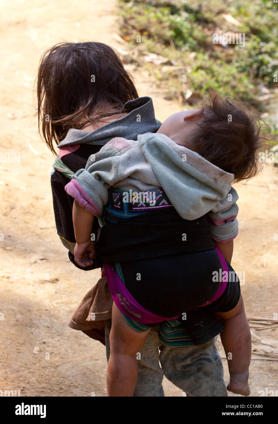 Young Vietnamese child carrying a smaller child in a sling on her back ...
