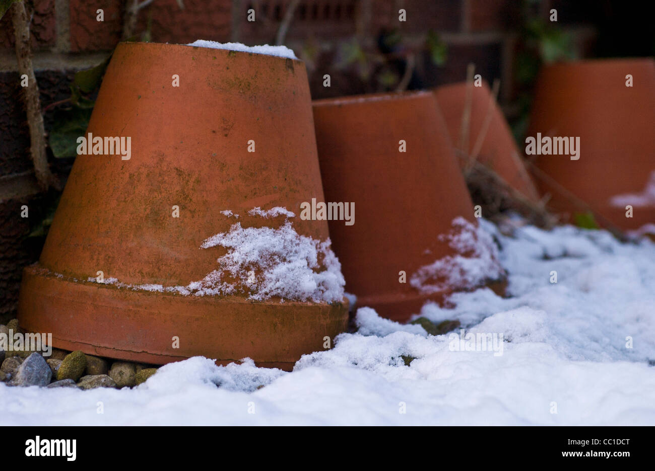 A row of upside down terracotta plant pots in snow, next to a brick ...