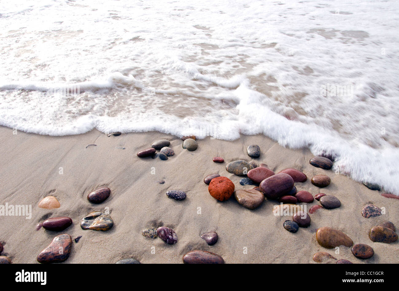 Sea waves beating stones lying in sea sand on coast line Stock Photo ...