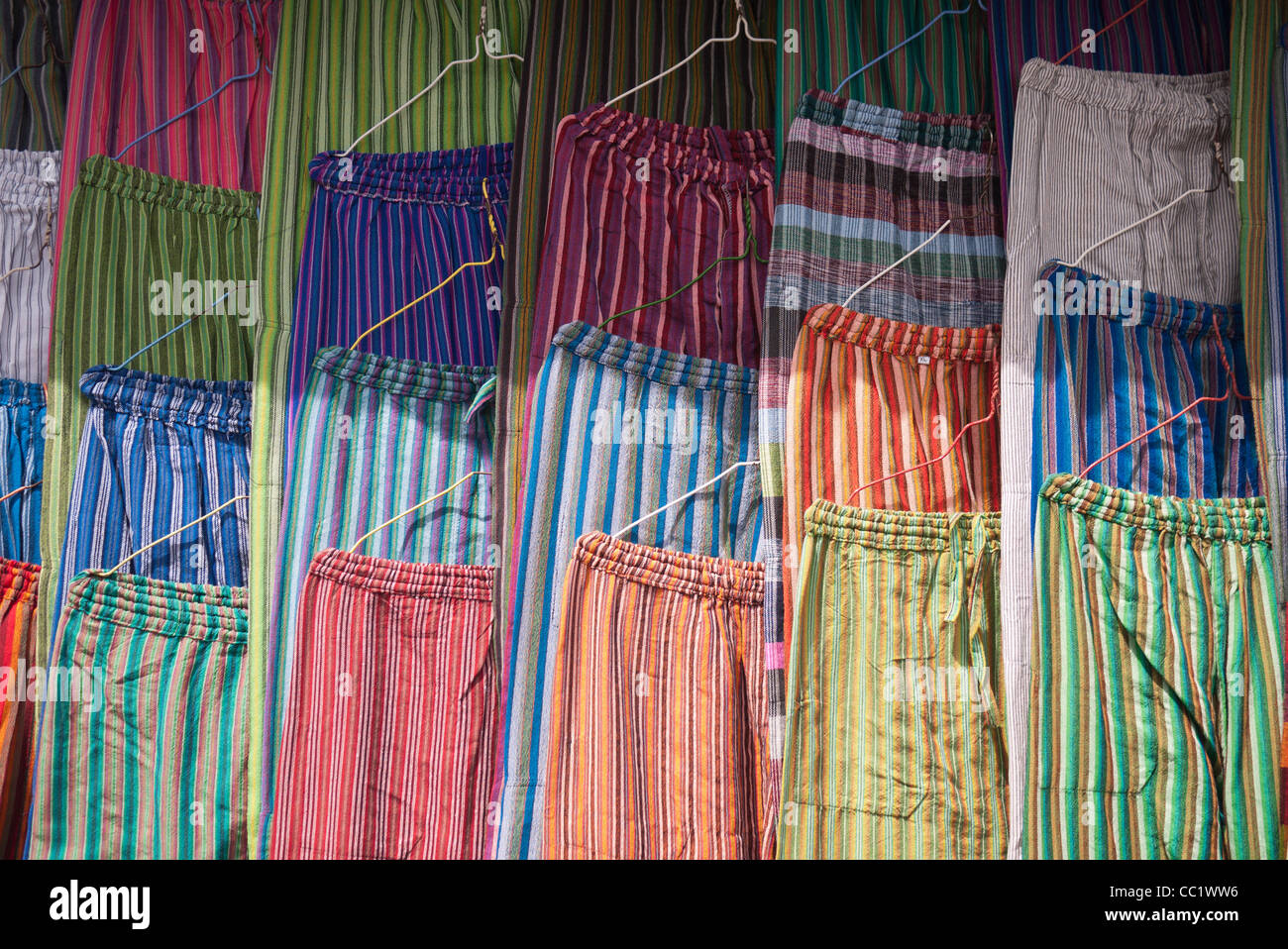 A variety of very colorful cloth pants hang in a display at the market ...
