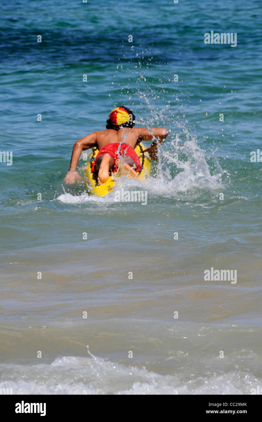 A young lifeguard springs into action with his surfboard to rescue a ...