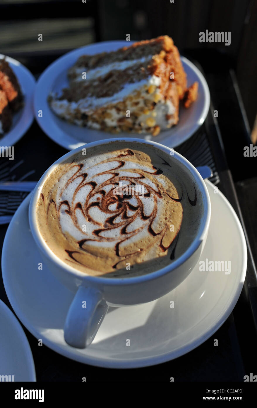 A cup of Cappuccino coffee with pattern drawn in froth and a slice of ...
