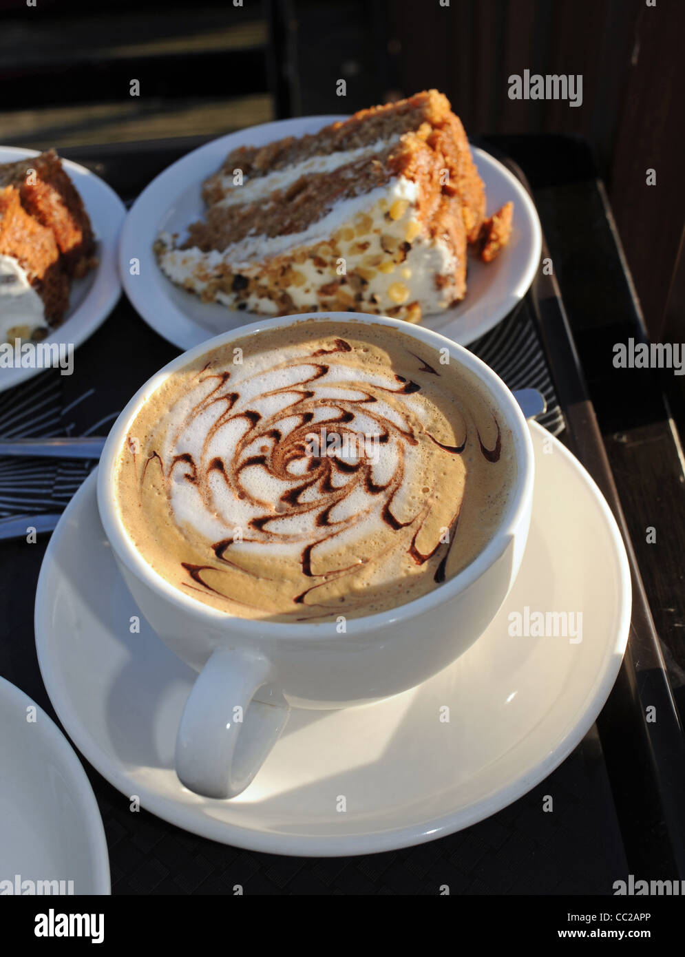 A cup of Cappuccino coffee with pattern drawn in froth and a slice of ...