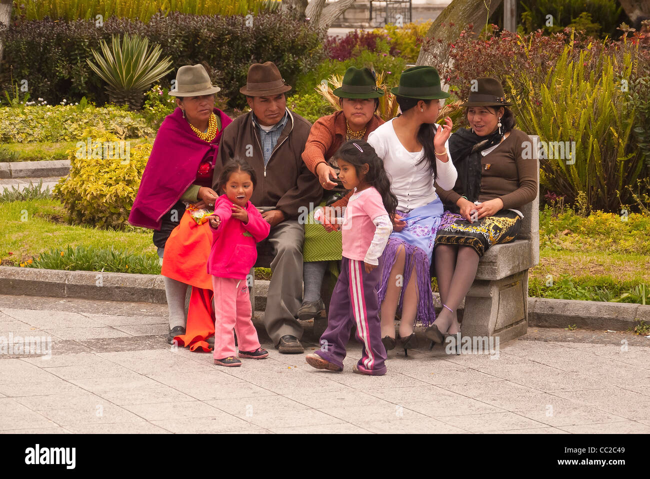 A family group of indigenous people from Ecuador sit together on a park ...