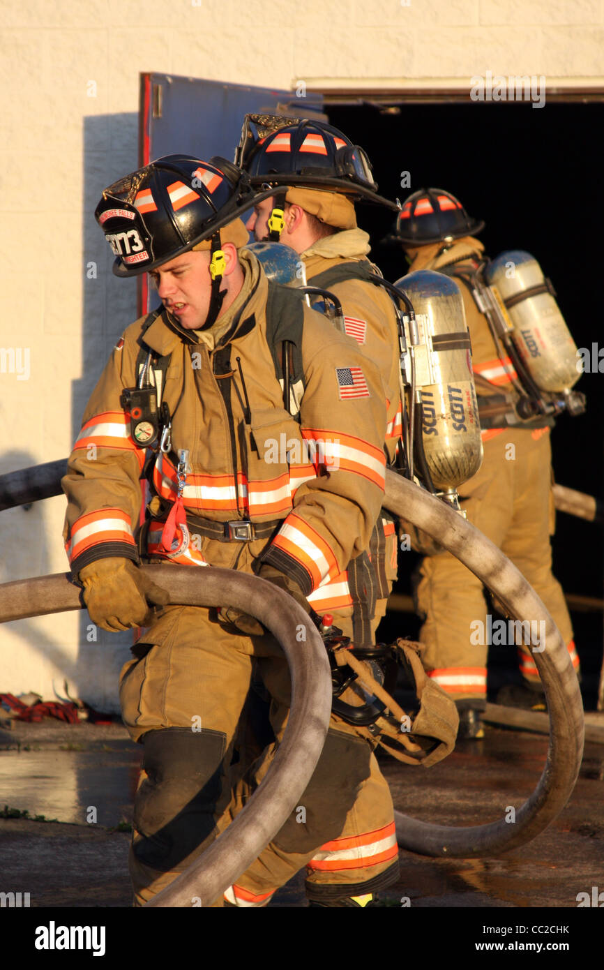 Three firefighters feeding hose into a building for search and rescue ...