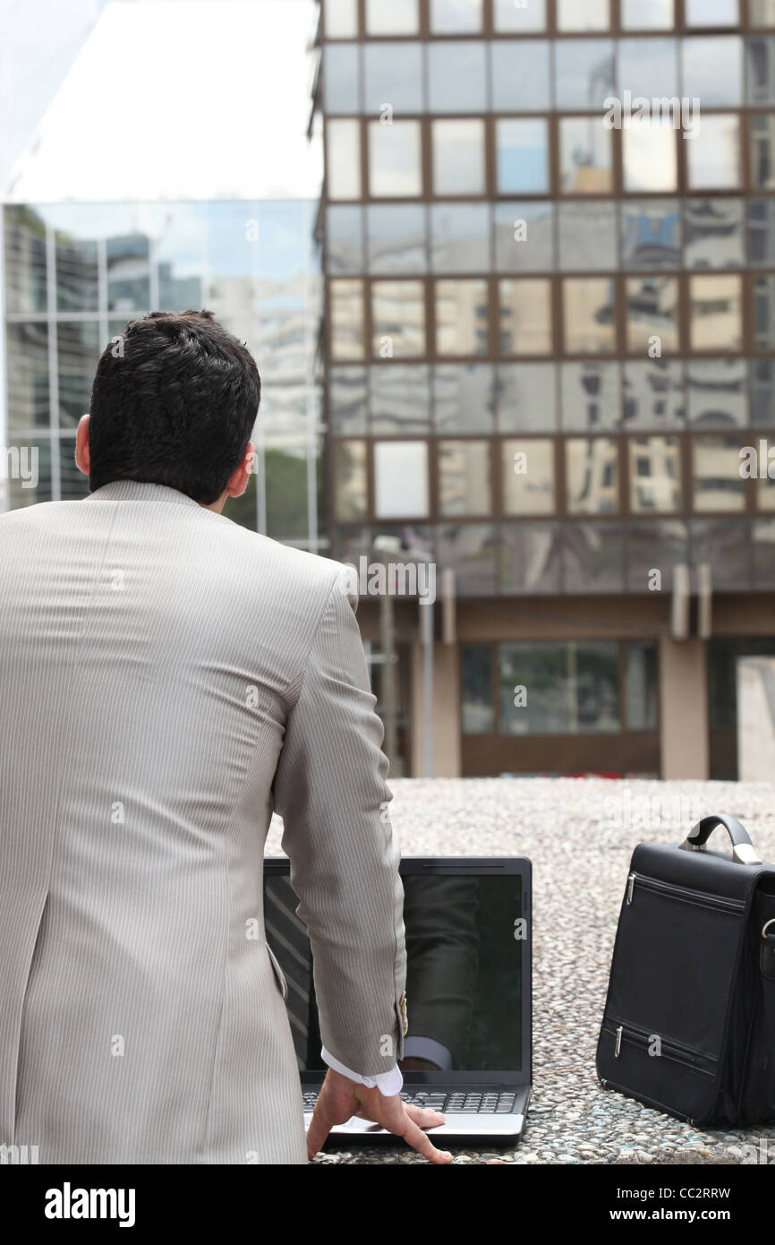 Back view of a businessman standing outside with computer and briefcase ...