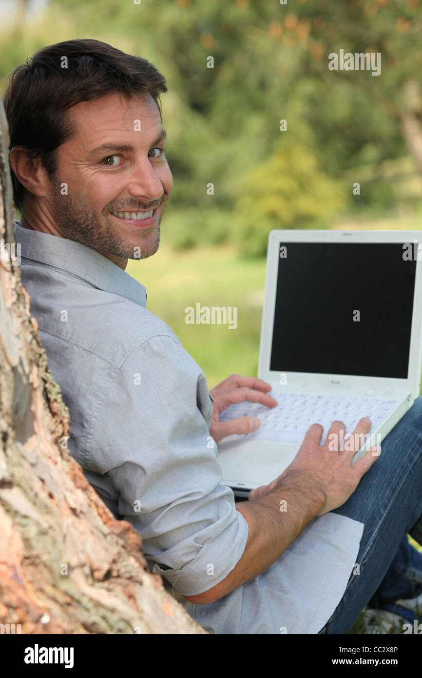 Happy man sitting outdoors using a laptop computer with a screen left ...