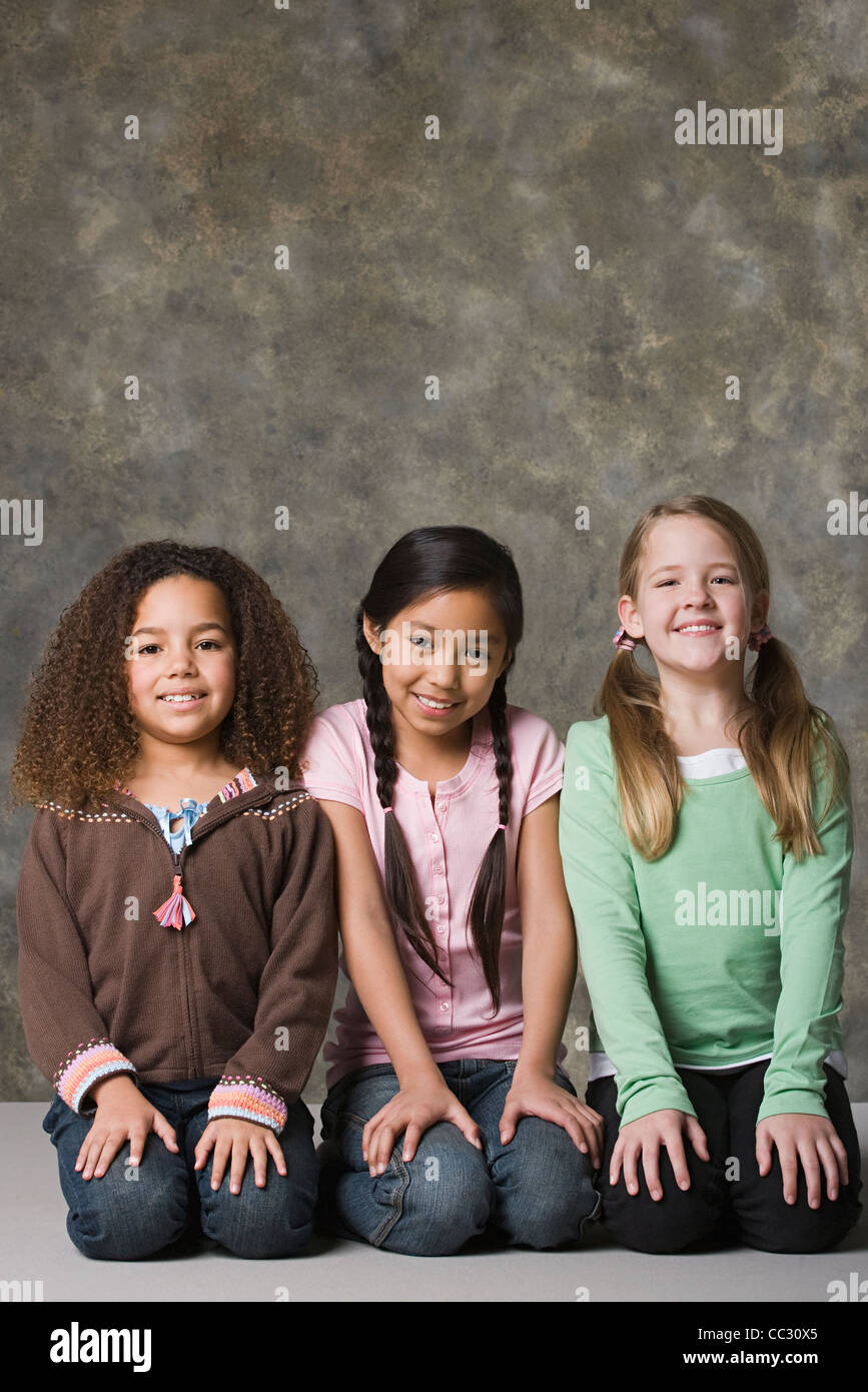 Portrait of three smiling girls (8-9) sitting together, studio shot ...