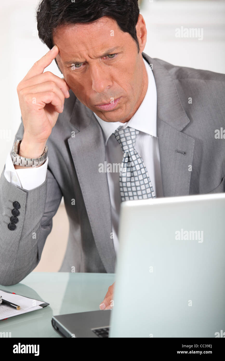 Businessman with a puzzled expression looking at a computer screen ...