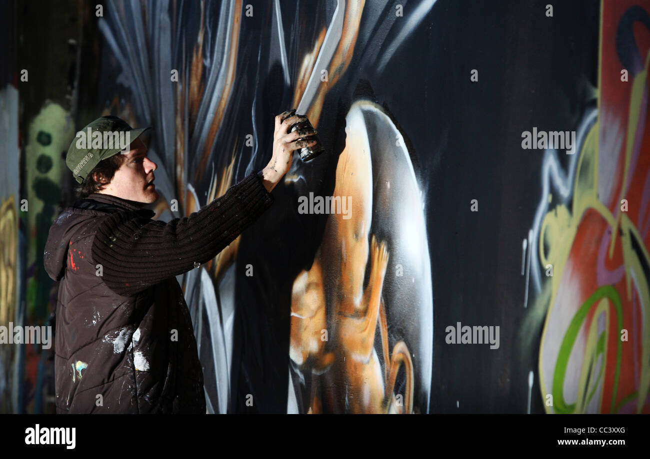 A graffiti writer spray painting a wall as part of a large scale mural ...