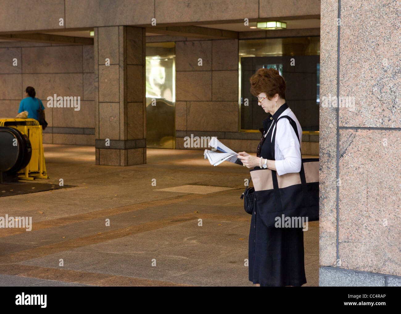 An elderly Caucasian woman reading a newspaper next to a building Stock ...