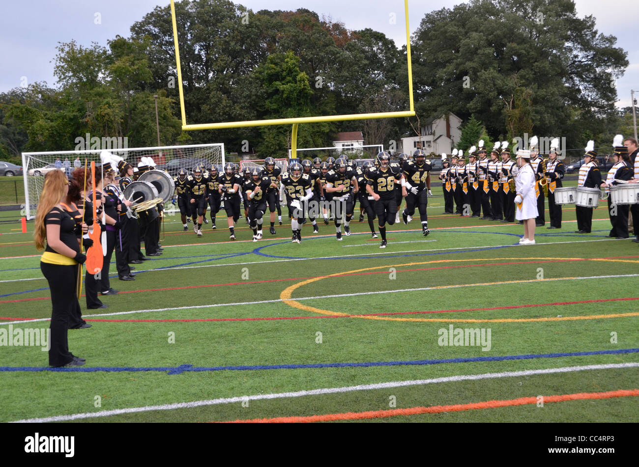 High school football team runs on the field while band and cheerleaders ...