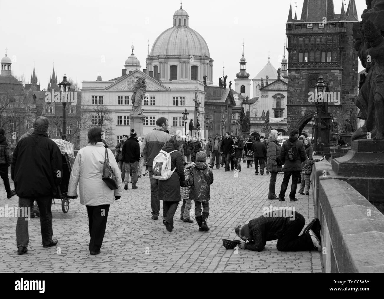 Homeless man begging on Charles Bridge with tourist walking by ignoring ...