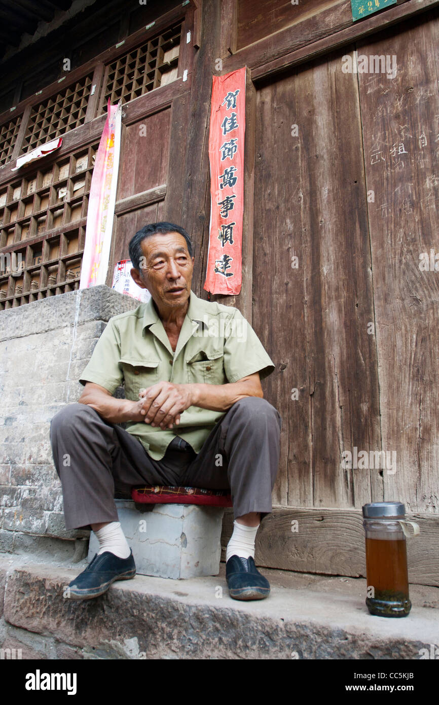 Elderly man sitting before traditional house, Qikou Old Town, Lvliang ...