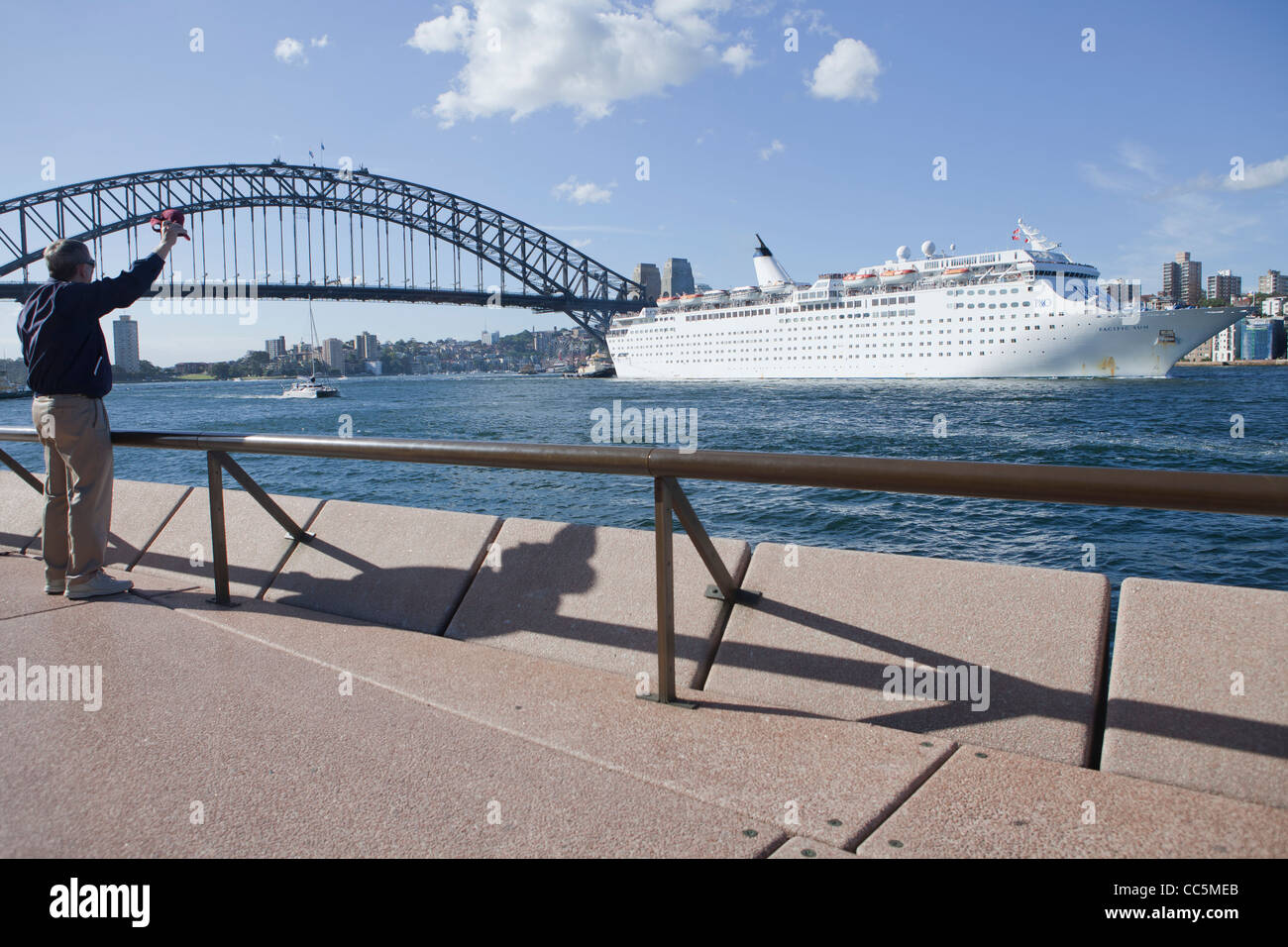 A man waving at a cruise ship traveling under the Sydney Harbour Bridge ...