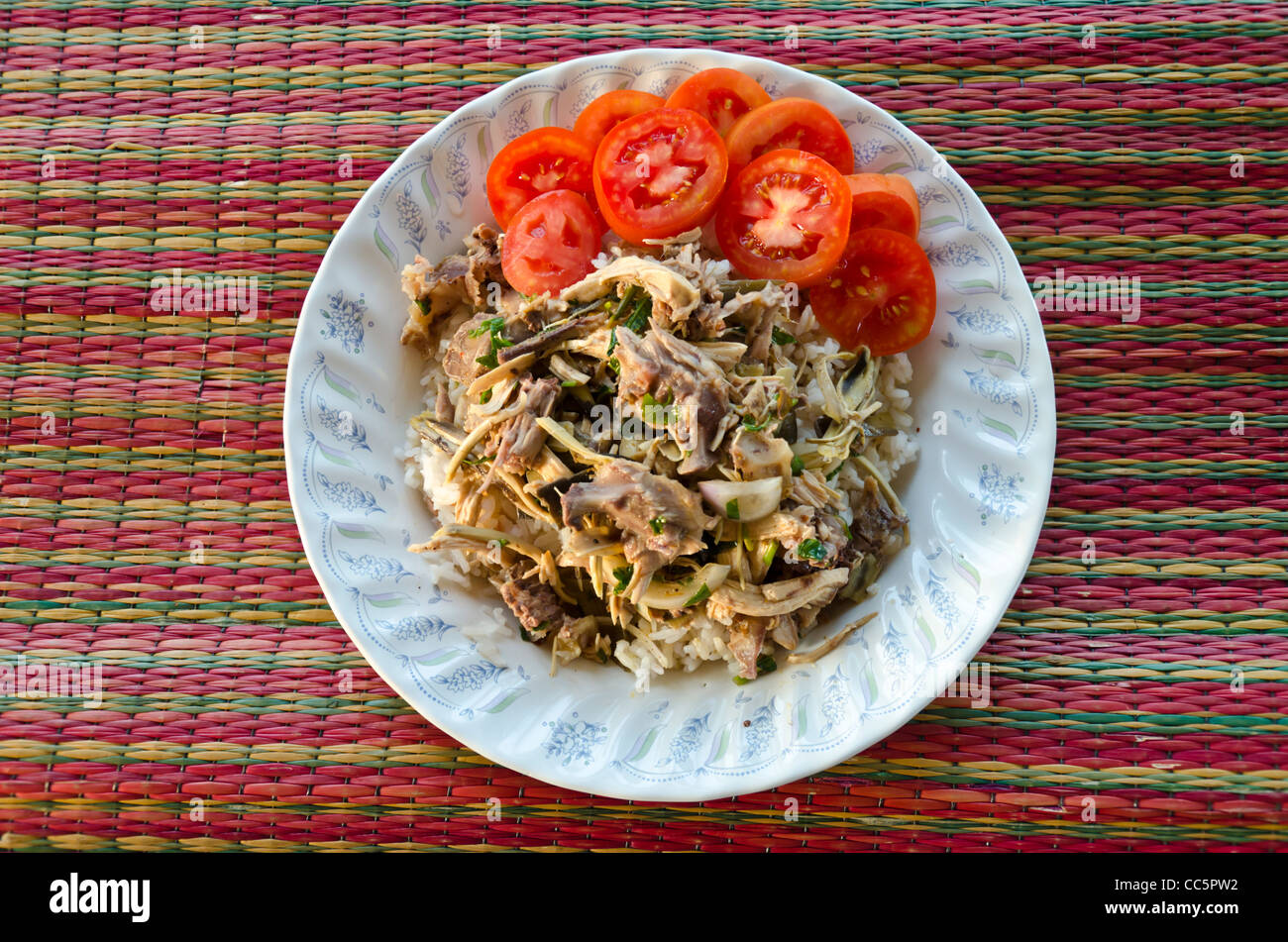 Plate with stir fried Thai food & sliced tomatoes on a woven straw mat ...
