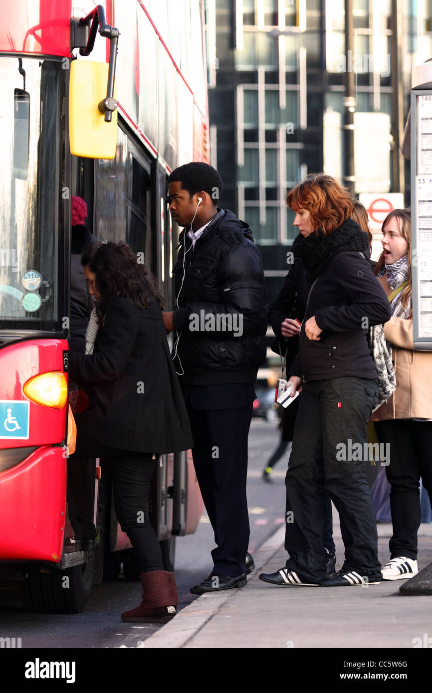people in a queue boarding a red London bus at a bus stop in London ...