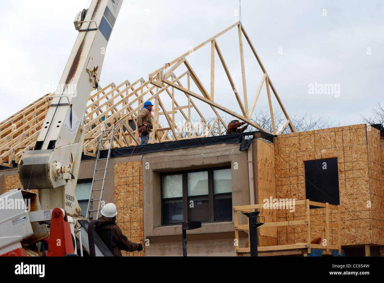 Crane operator lifts prefabricated rafter onto wood frame roof Stock ...