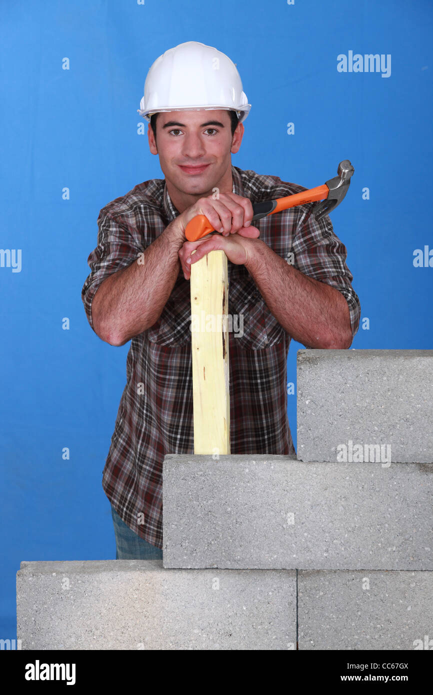 Builder with hammer and timber next to a block wall Stock Photo - Alamy