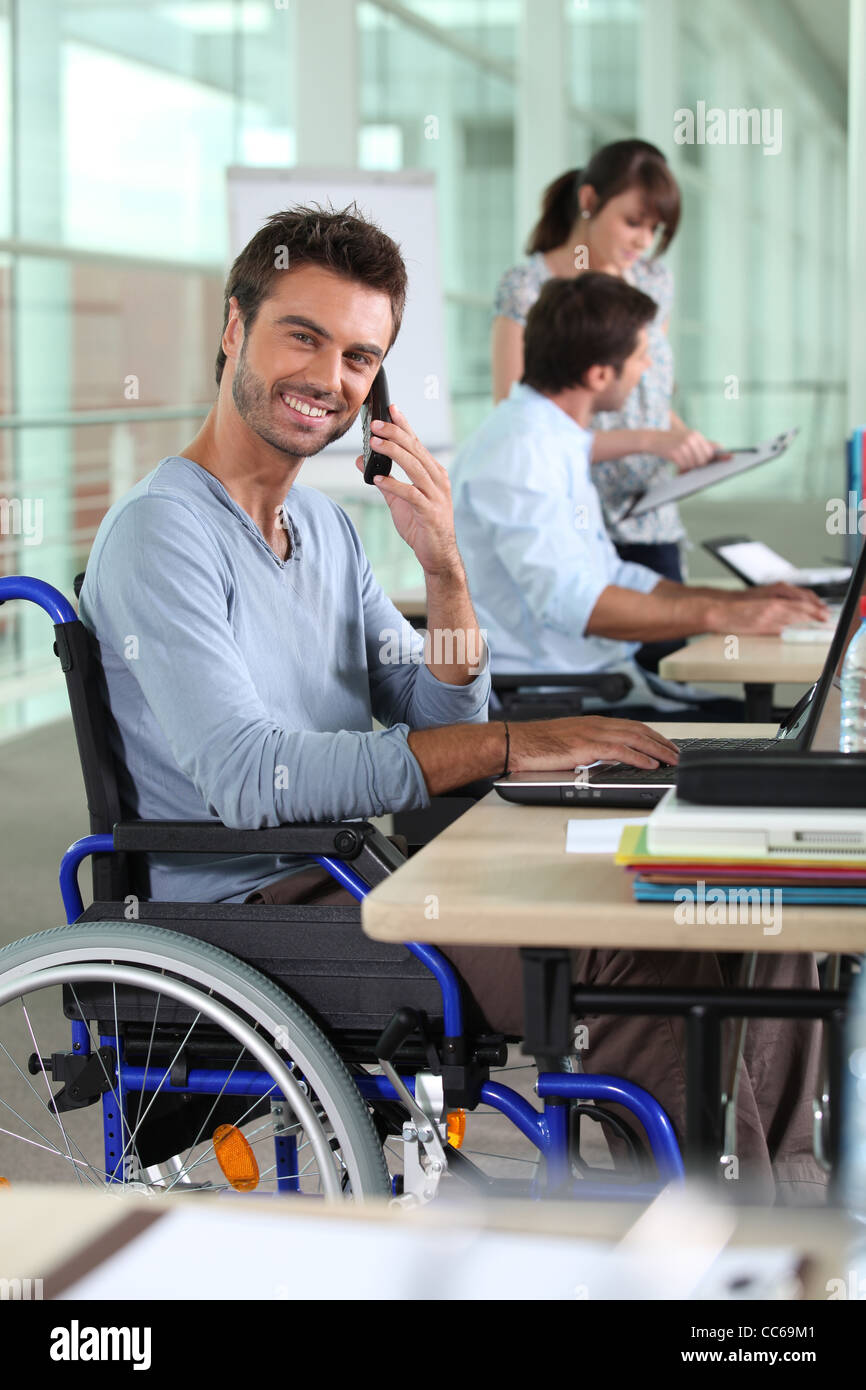 Smiling man in a wheelchair working in an office Stock Photo - Alamy