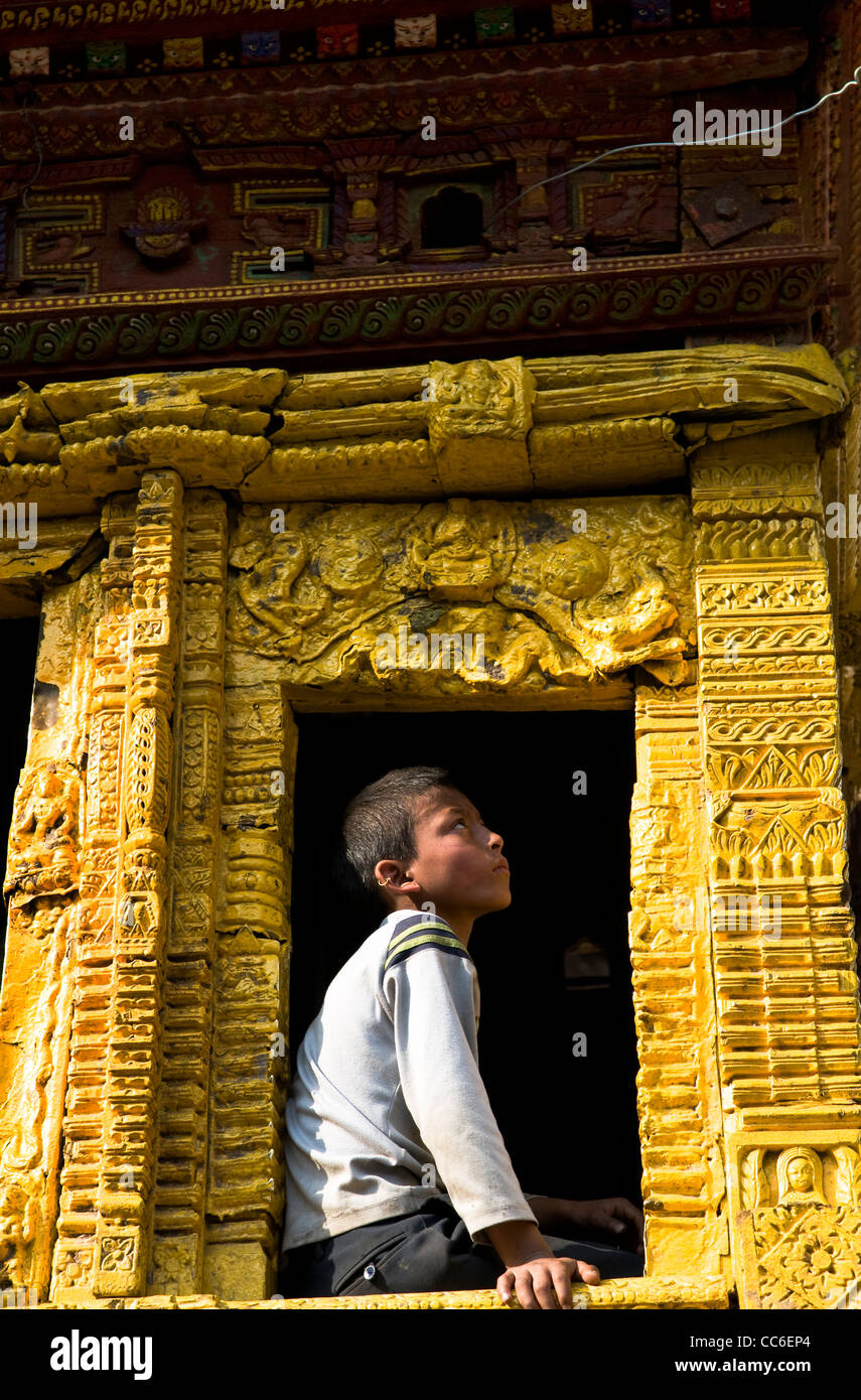 A boy sitting on a window of a golden wooden chariot used in Nepalese ...