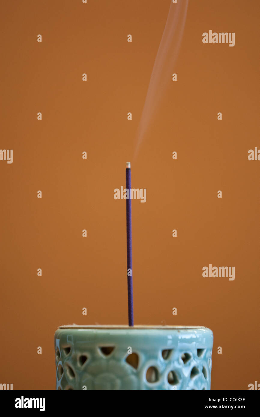 A stick of incense smolders and smokes in an incense burner pot Stock ...