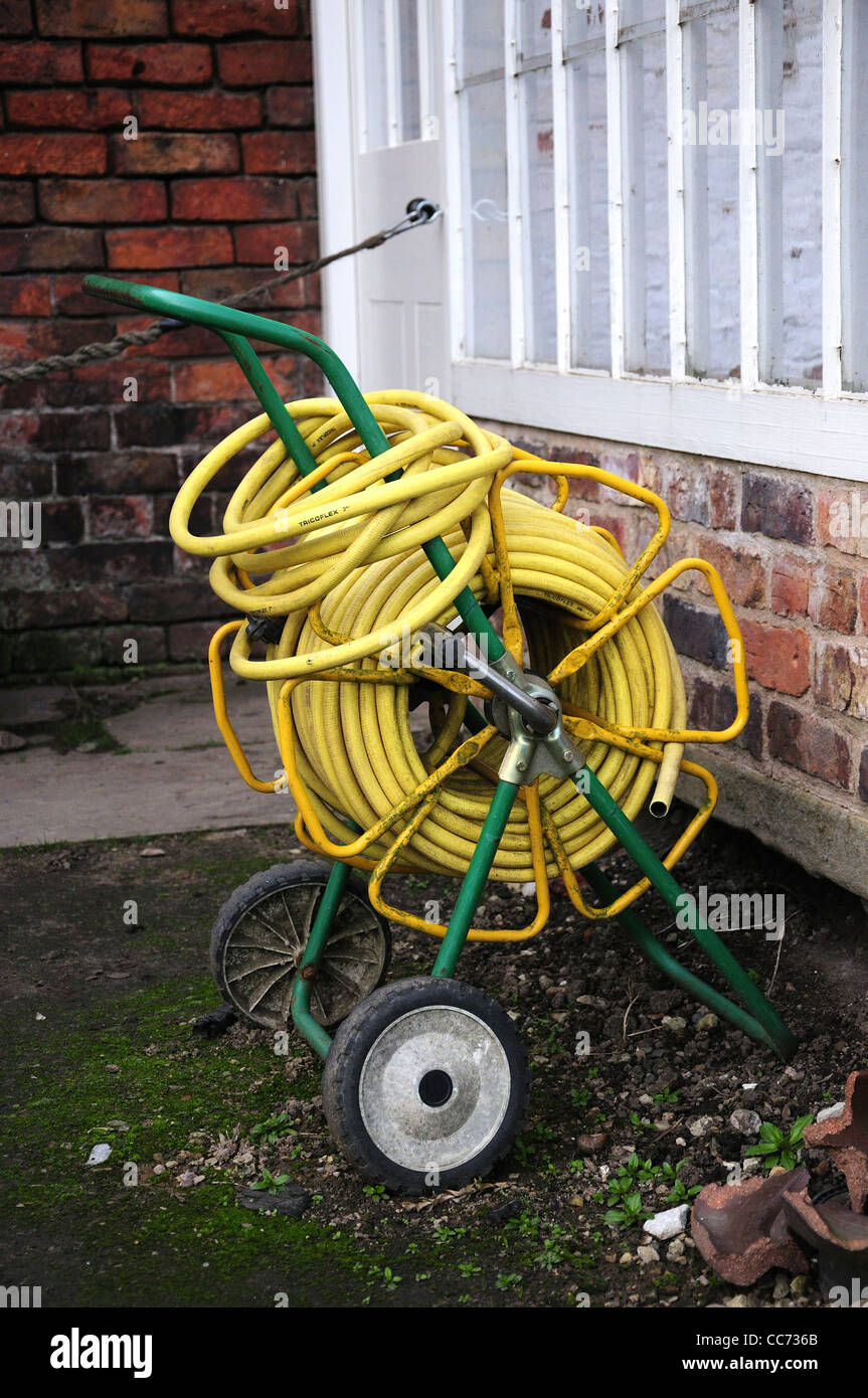 Small green wheeled hand trolley with coiled yellow hosepipe outside ...