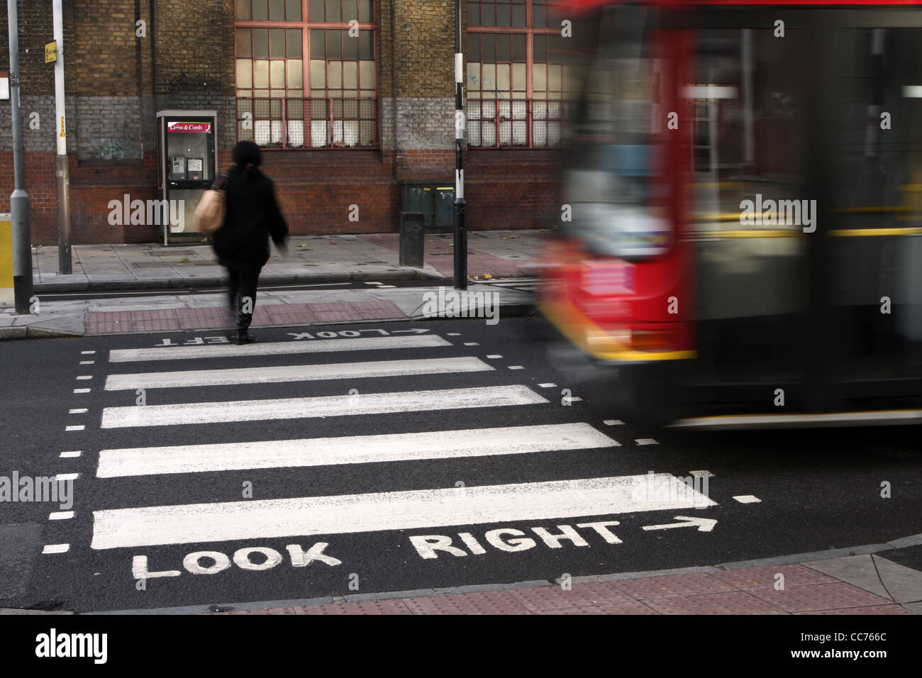 a female walks across a zebra crossing in London while a bus ...