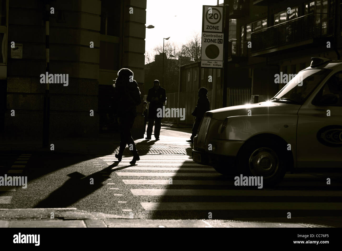 a lady walks across a zebra crossing and a taxi crosses the crossing ...